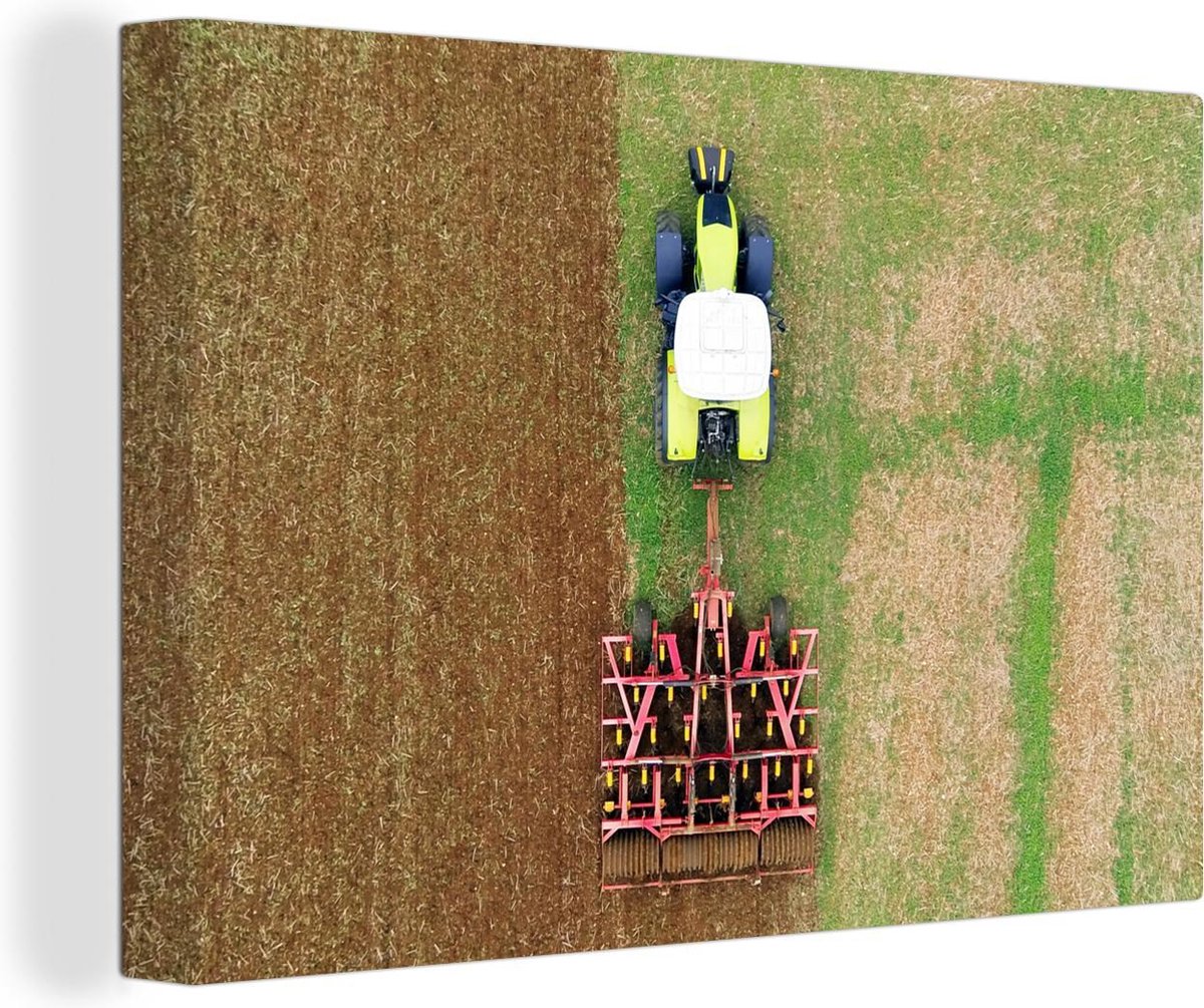 Canvas Schilderij Een trekker die met een ploeg het veld omploegt ...