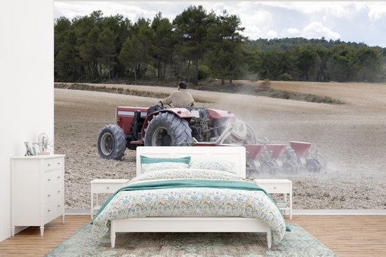 Behang - Fotobehang De boer ploegt zijn veld met zijn rode tractor ...